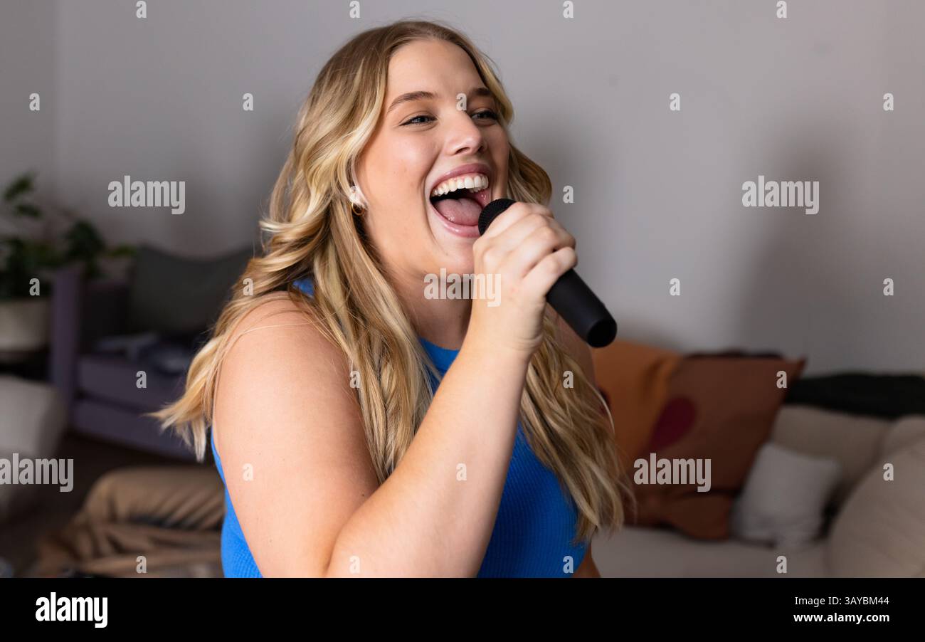 Young woman singing into black microphone in modern living room, with ...