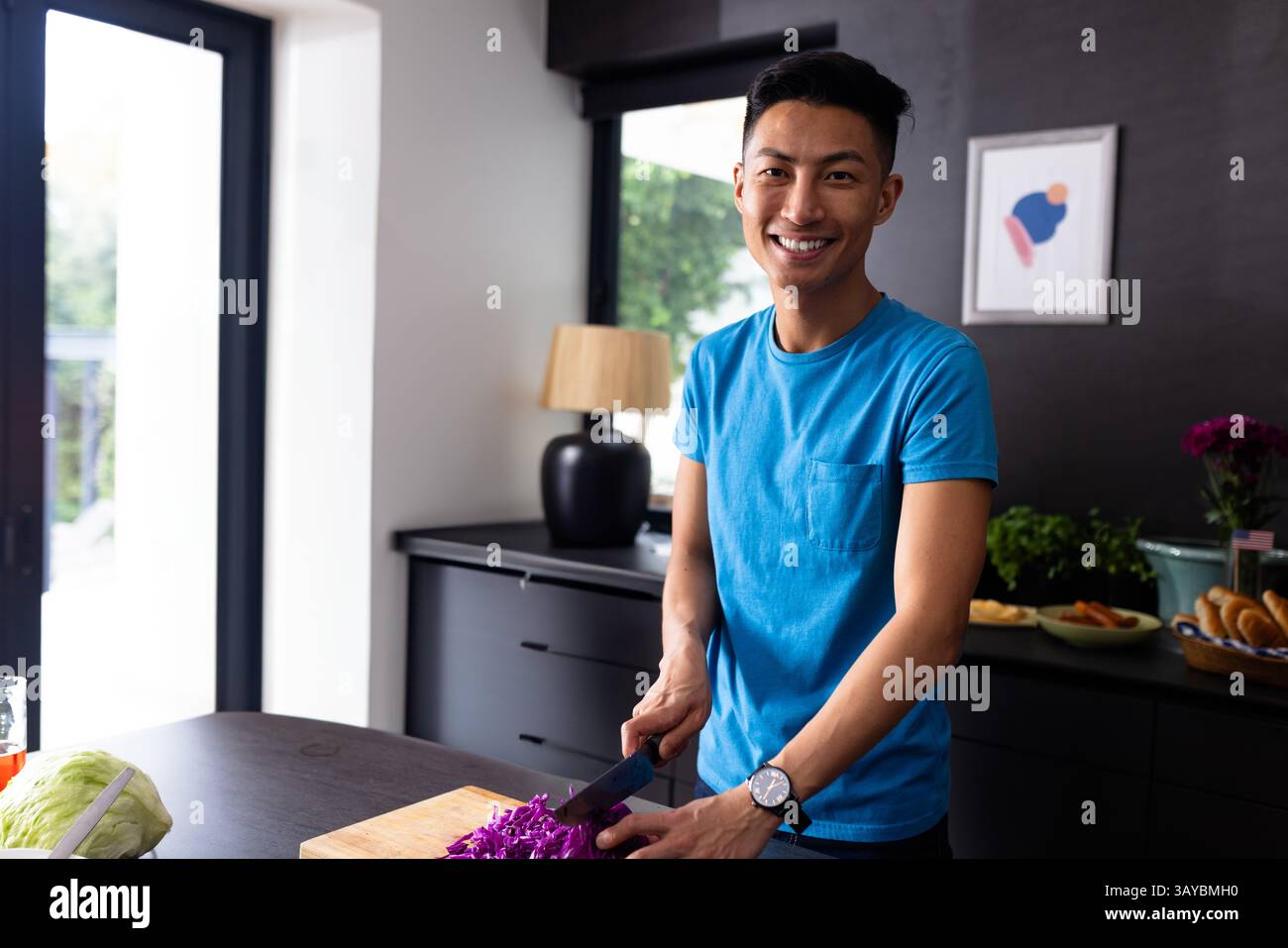 Asian man chopping purple cabbage on kitchen island in modern home ...