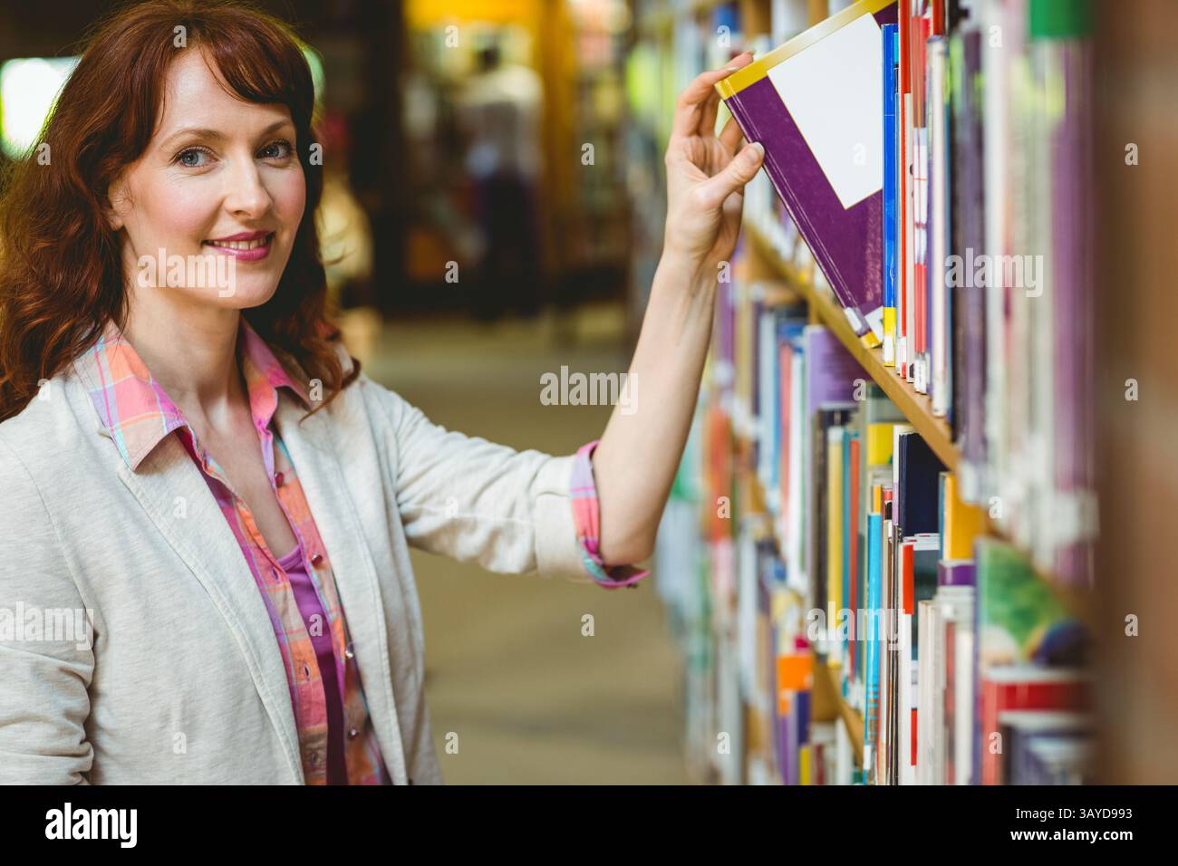 Woman selecting purple-covered book from tall wooden bookshelf in ...