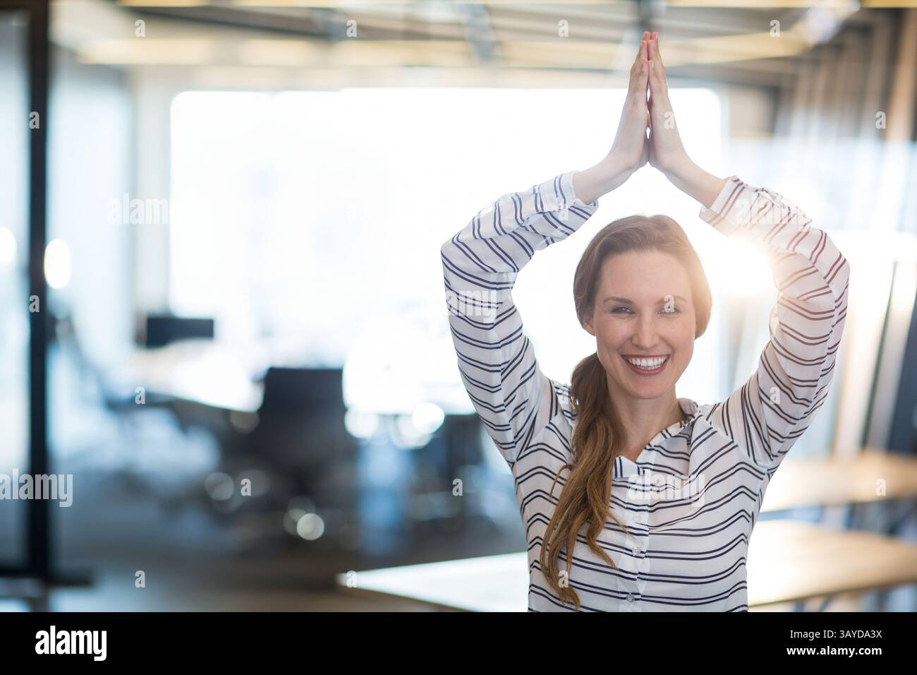 Business-casual woman stretching arms overhead in modern office with ...