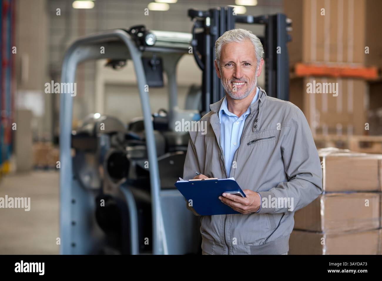 Senior man standing in warehouse holding clipboard and pen near ...