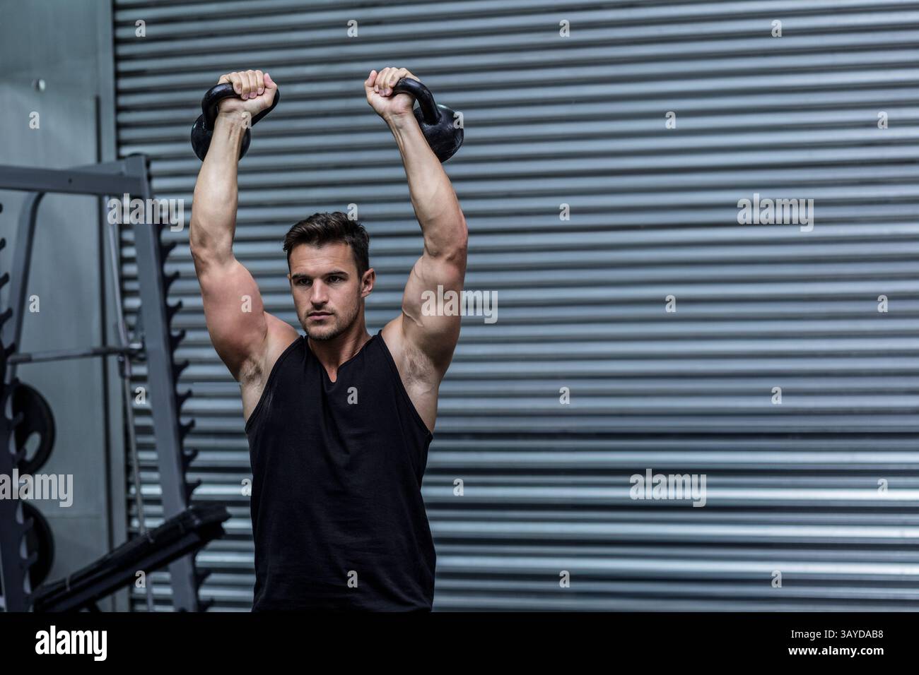 Man lifting kettlebells overhead at industrial-style gym, with weight ...