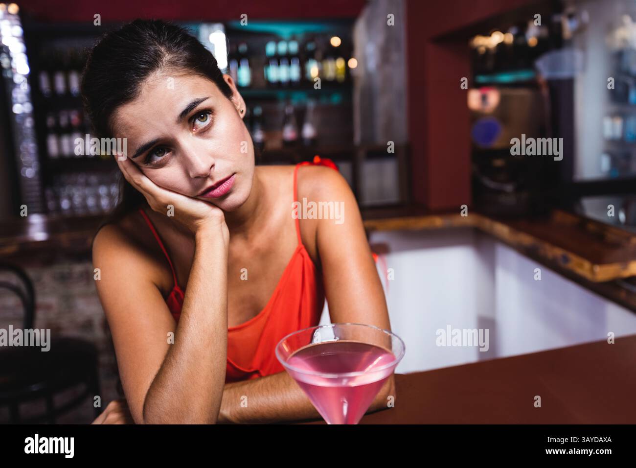 Woman resting head on hand and gazing upward at bar counter, with pink ...