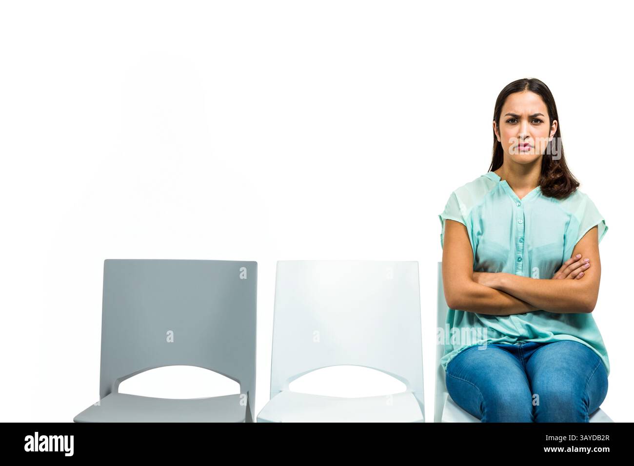 Woman sitting on plastic chairs in empty studio, crossing arms, legs with stern look, copy space ...