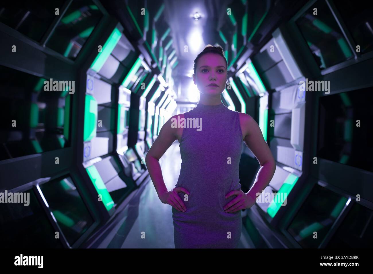 Young woman standing in high-tech corridor with glowing hexagonal frames, expressing confidence ...