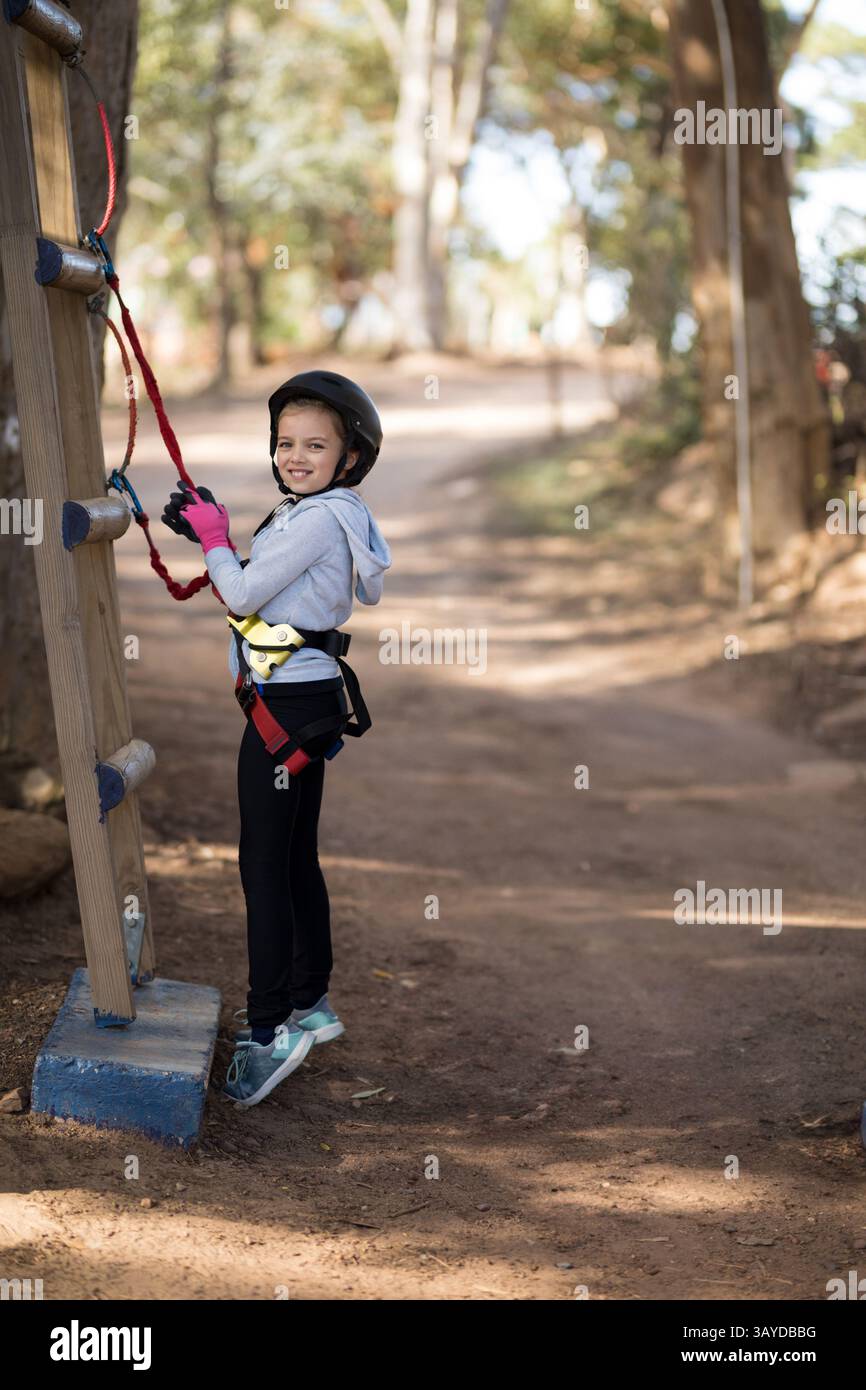 Girl climbing wooden ladder in forest adventure park, with helmet ...