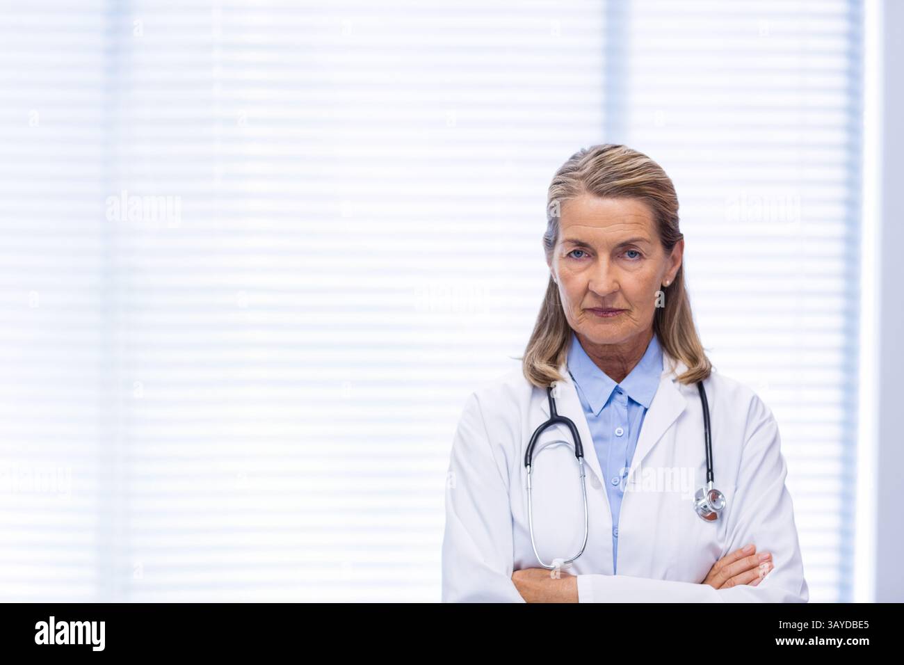 Senior female doctor standing facing camera in clinic, with stethoscope and lab coat, copy space ...
