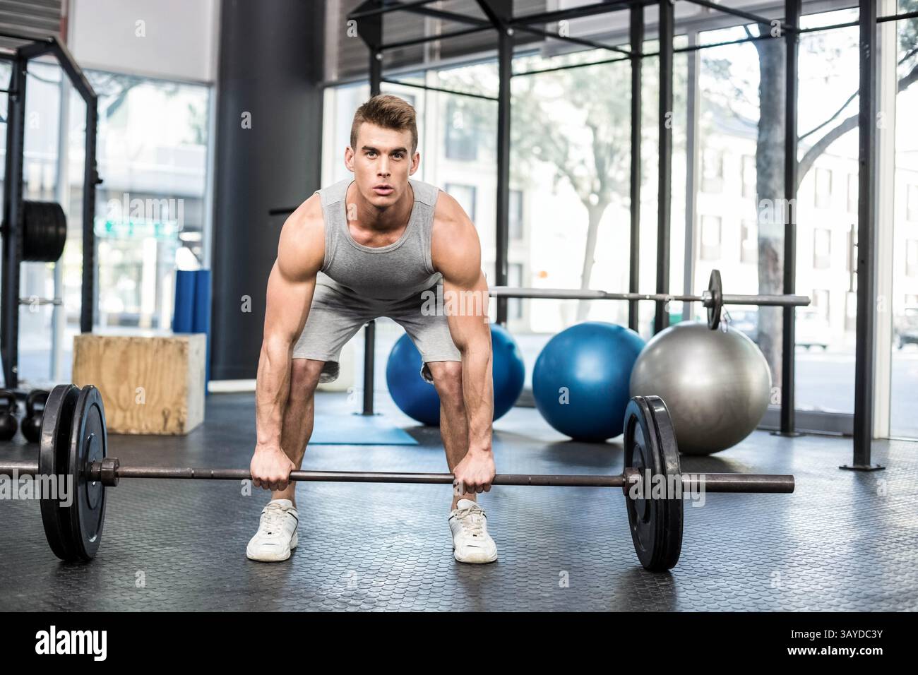 Muscular man lifting loaded barbell in modern gym, with rubber flooring ...