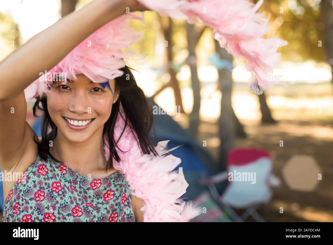 Mid adult Asian woman lifting pink feather boa overhead in park with ...
