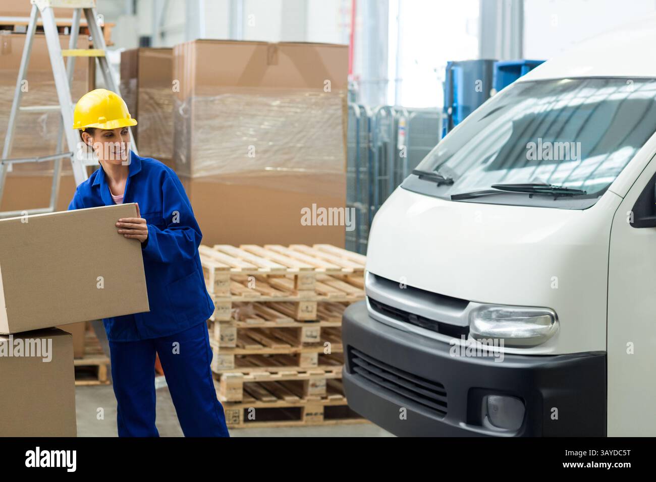 Young woman lifting cardboard box at loading dock, stacking pallets by ...