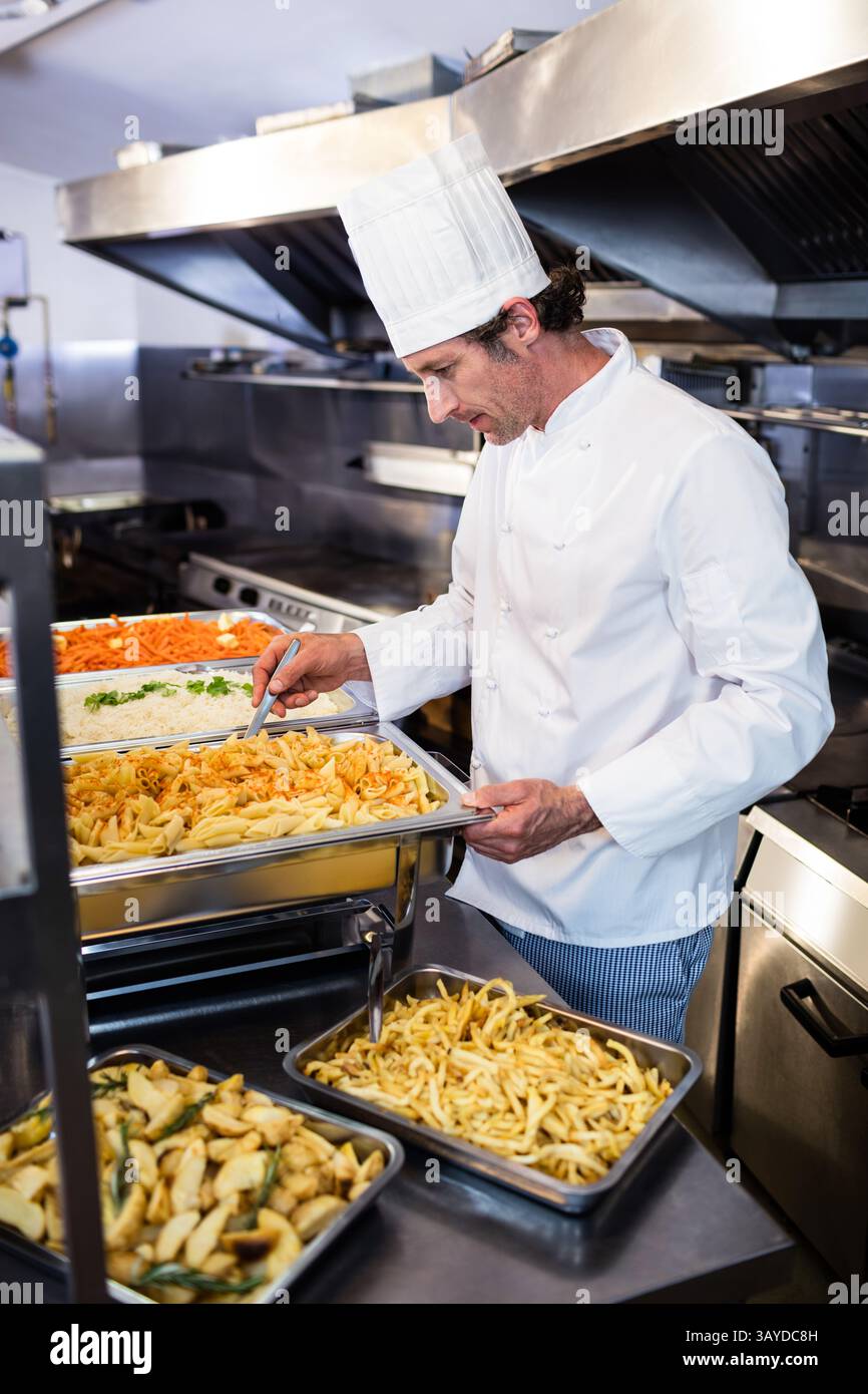 Male chef plating pasta and fries from buffet trays in commercial ...