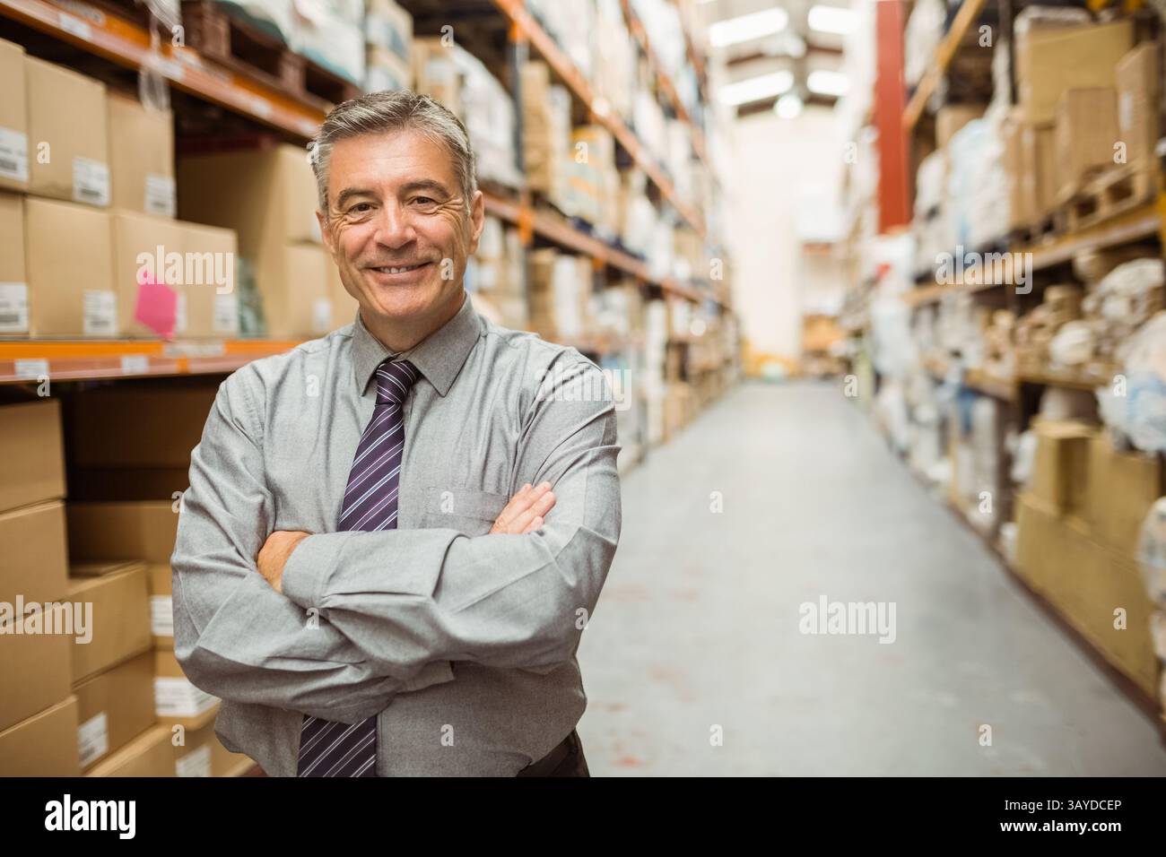 Man standing in warehouse aisle wearing shirt and tie, smiling among ...