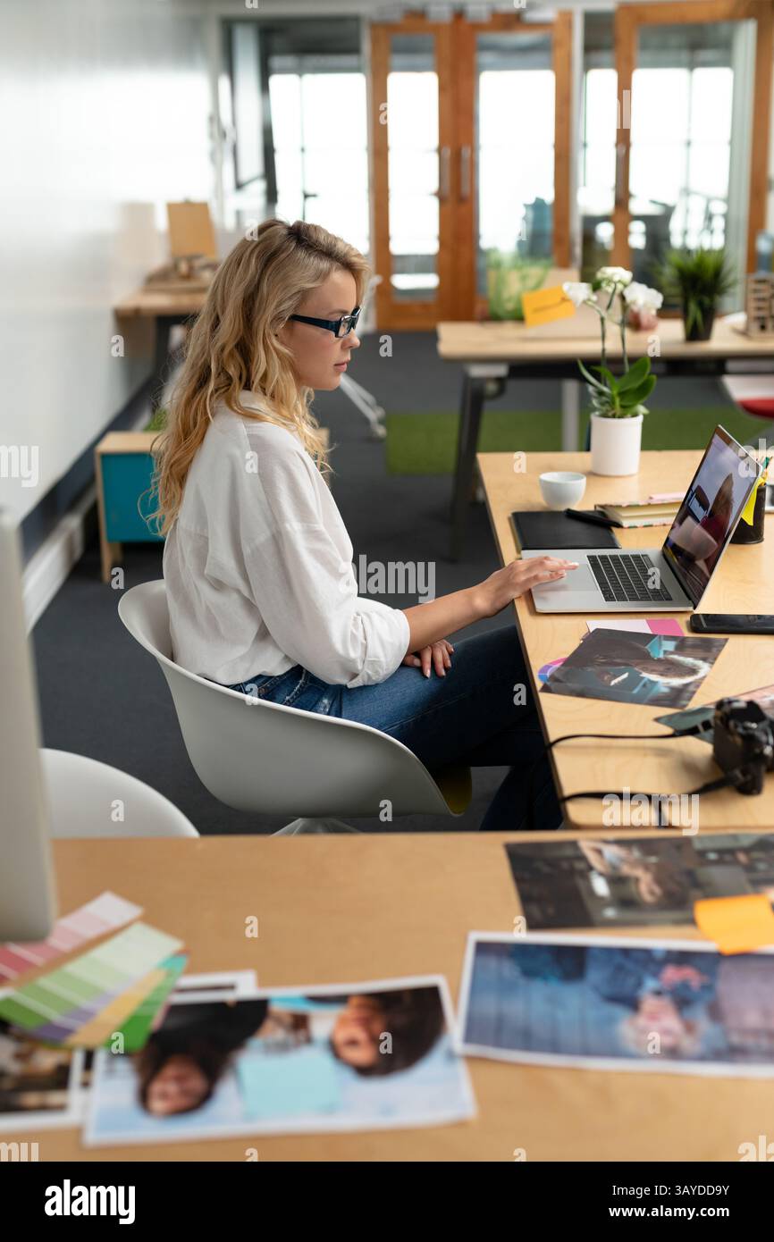 Woman focusing on laptop in modern office with printed photographs and ...