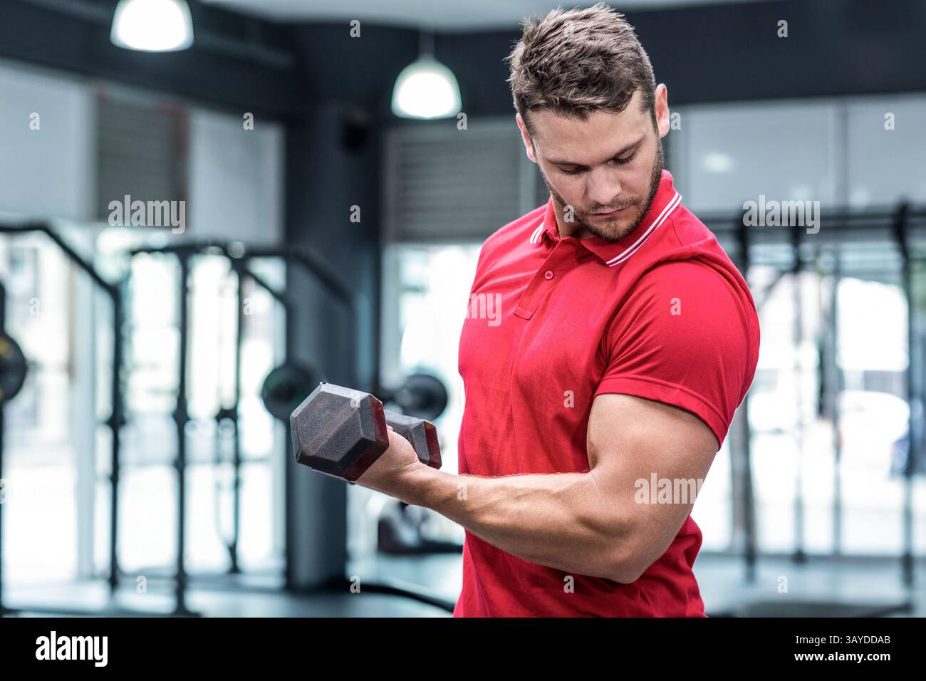 Young adult man curling hex dumbbell in modern gym with weight racks ...