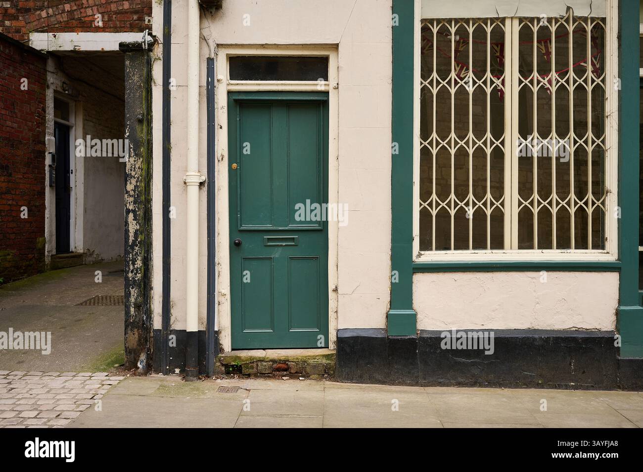old disused shop front with green door and metal shutters on window and ...