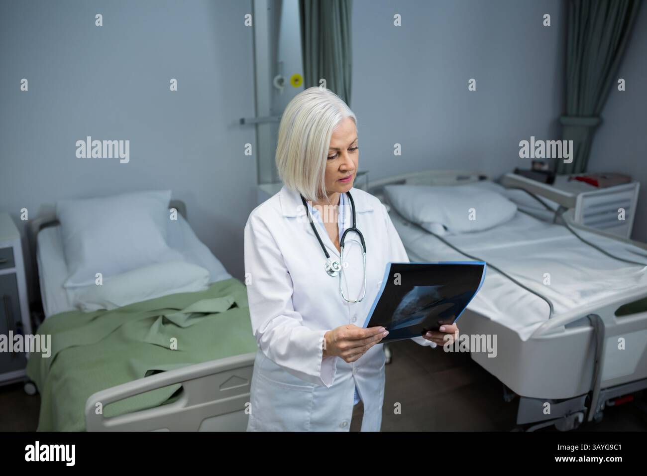 Female doctor examining X-ray film in hospital patient room, with two ...