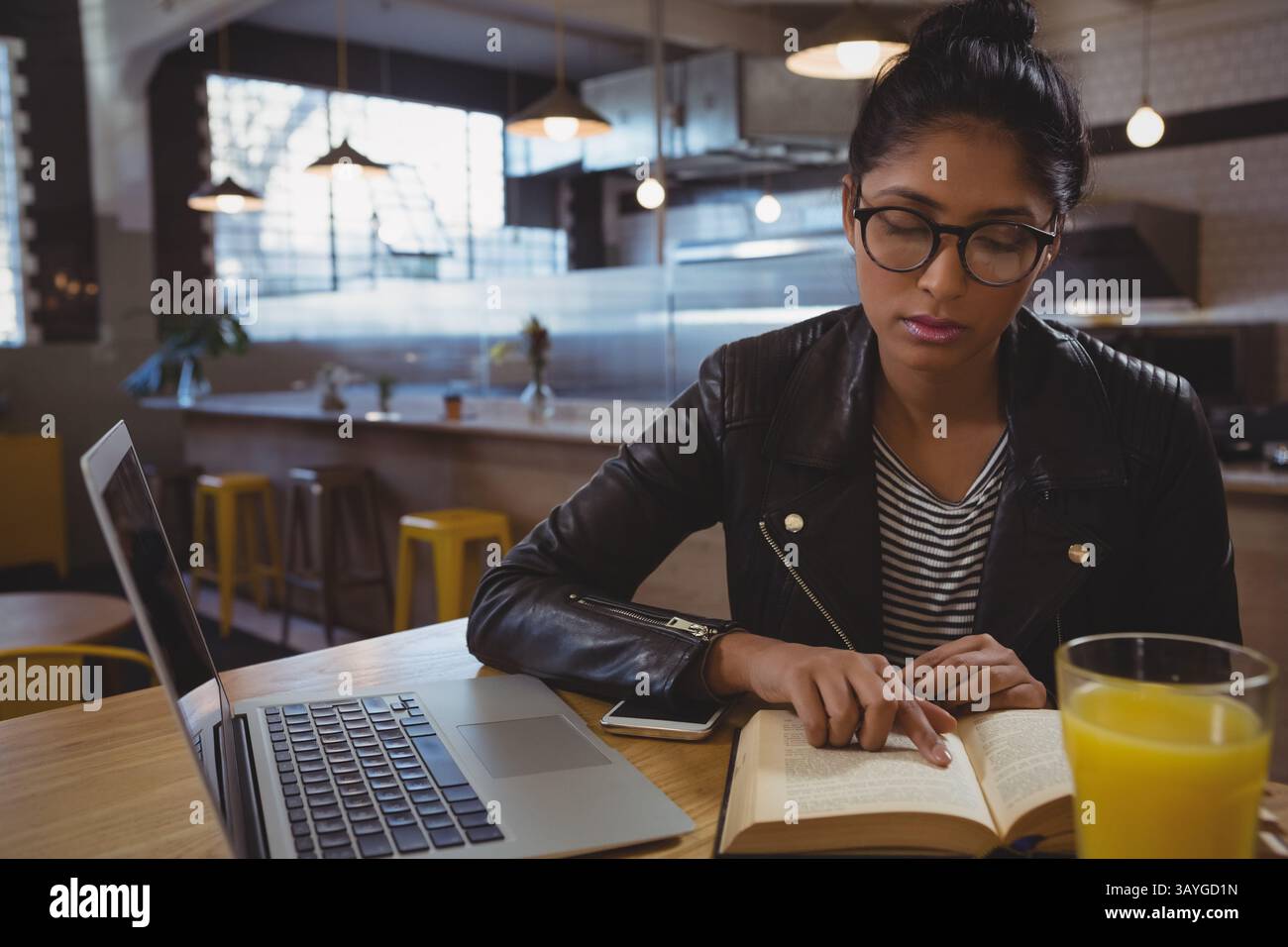 Indian woman reading open book at cafe table, tracing text with finger ...