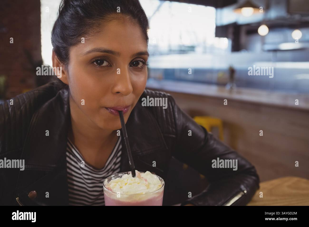 young Indian woman sipping pink milkshake at wooden café table, with ...