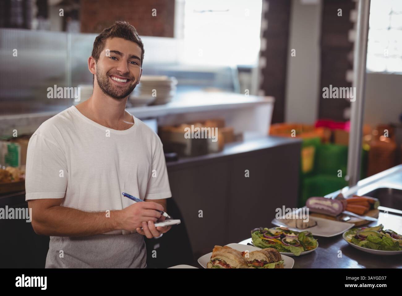 Young adult server taking order behind metal counter in deli, with pen ...