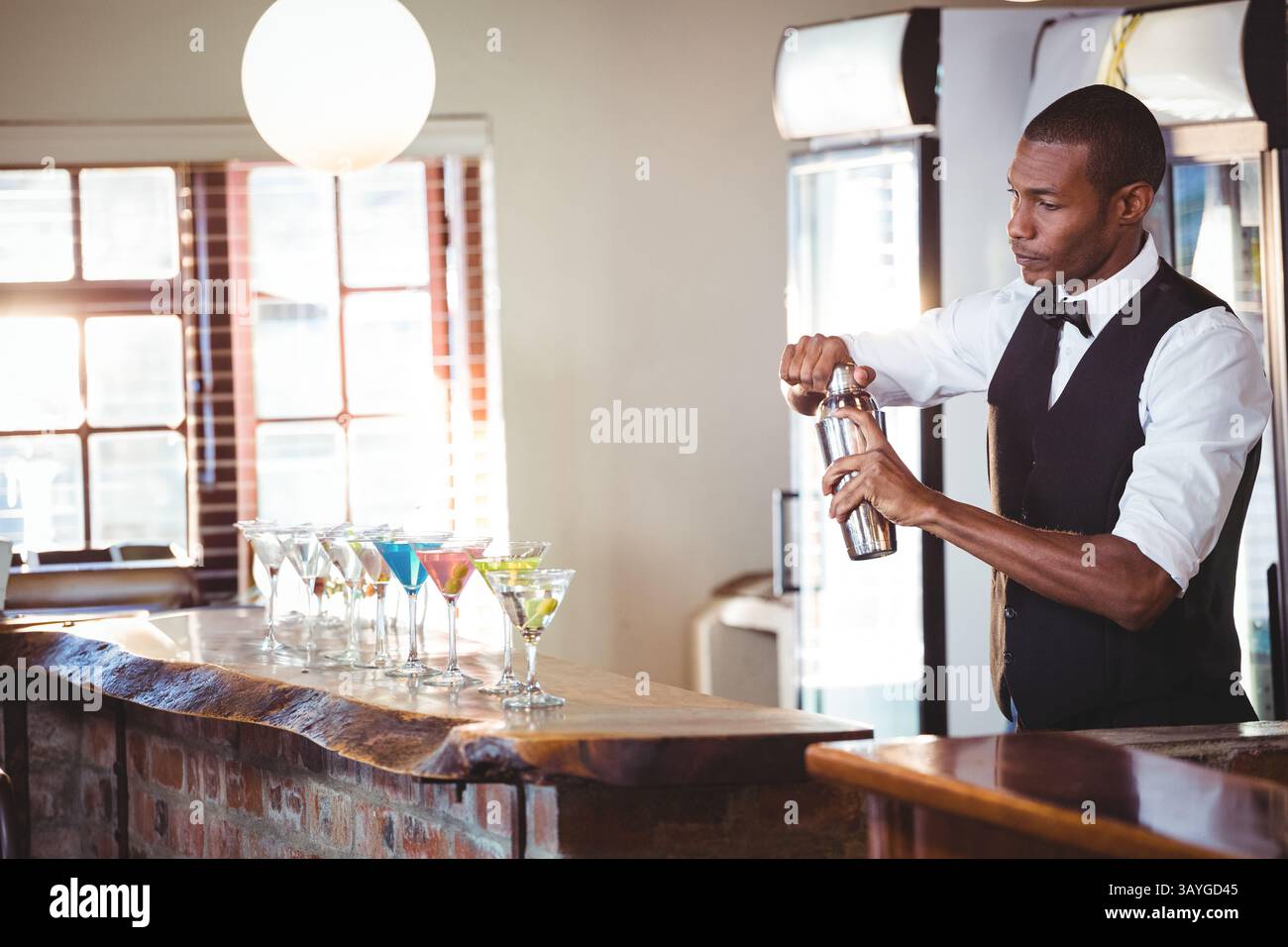 African American bartender shaking cocktail shaker behind wood bar with ...