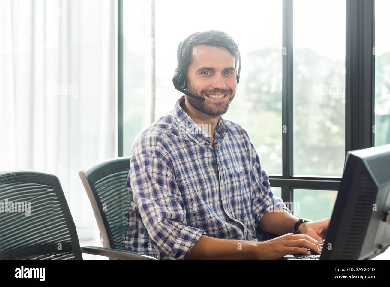 Man typing on keyboard in modern office at floor-to-ceiling windows ...