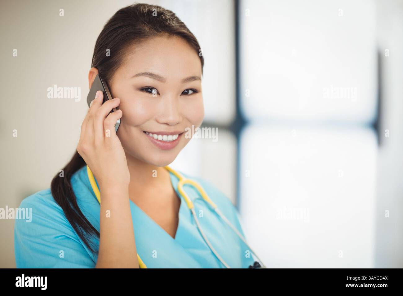 Asian female nurse talking on smartphone in clinic, with yellow ...