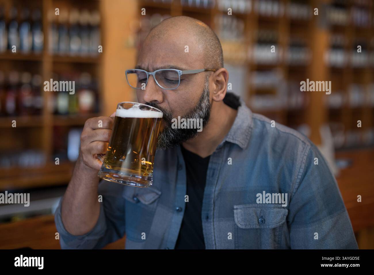 Indian man sipping beer from large glass mug at wooden bar counter ...
