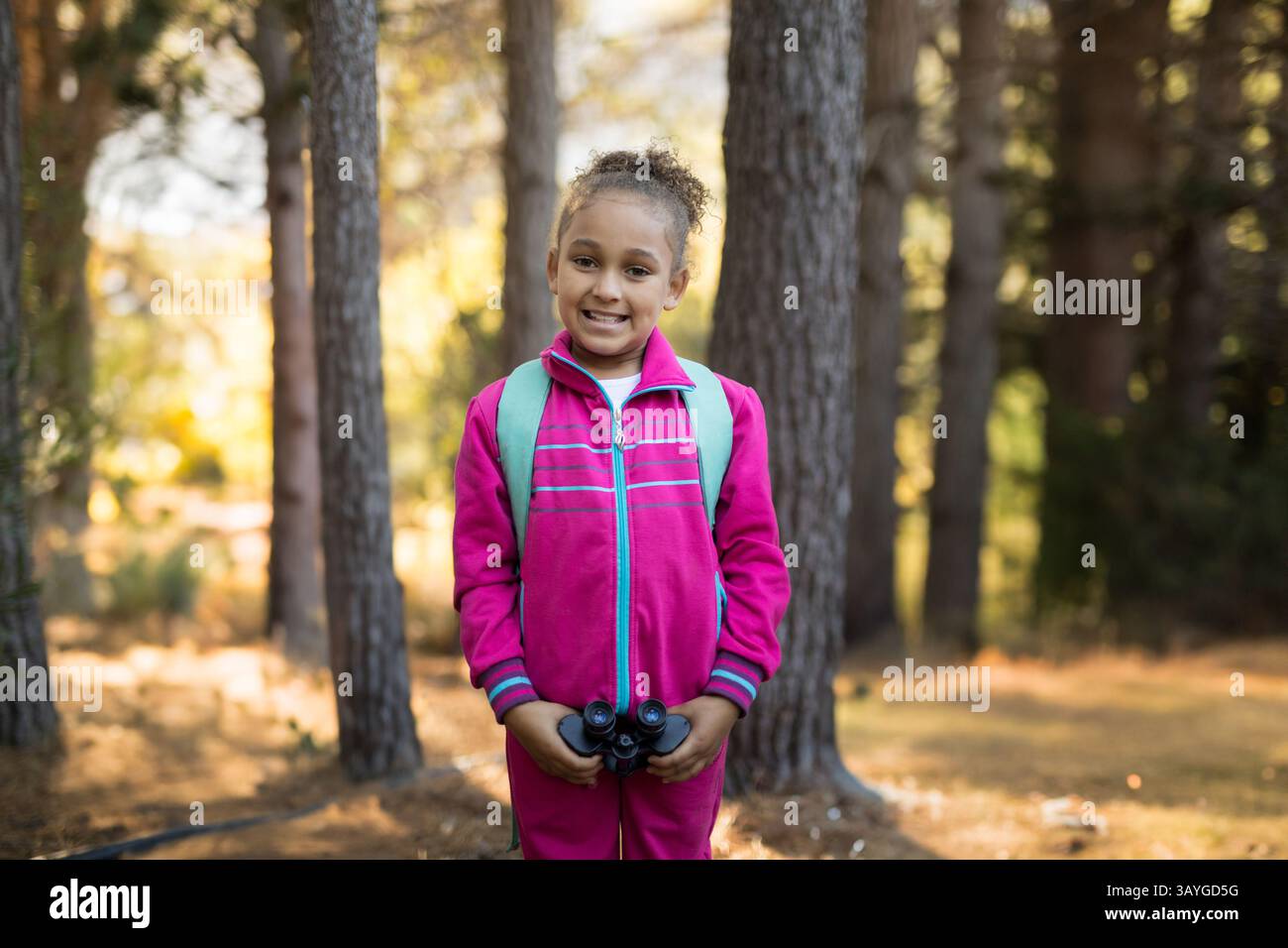 School-aged girl standing in pine forest wearing pink tracksuit ...