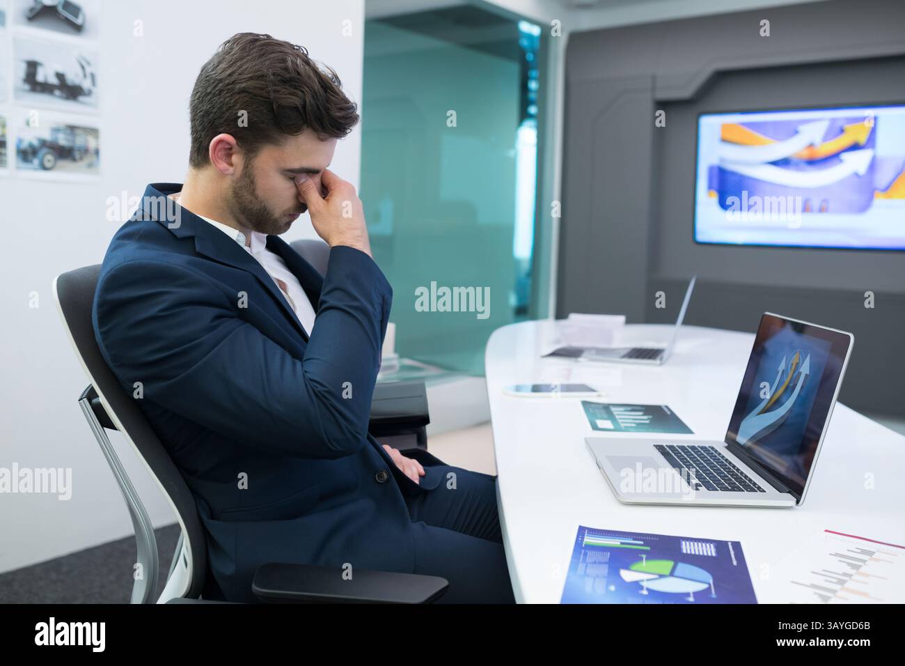 Young adult man pinching bridge of nose in conference room, with laptop ...
