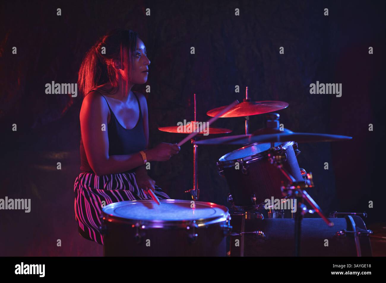 Young adult Asian female drummer performing on stage with drum kit ...