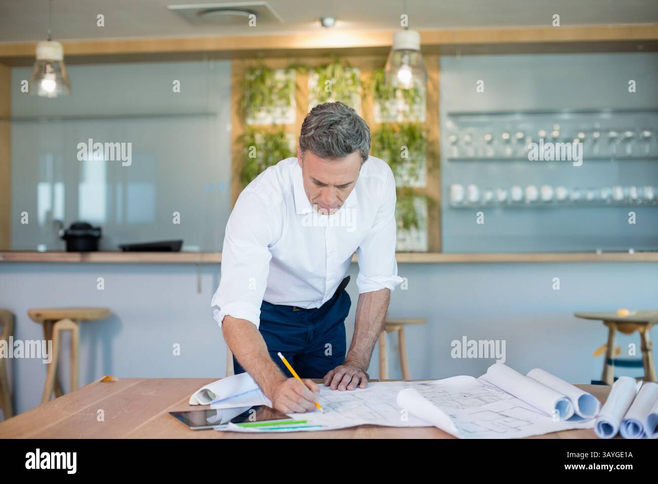 Middle-aged man sketching on blueprints in modern office kitchen, using ...