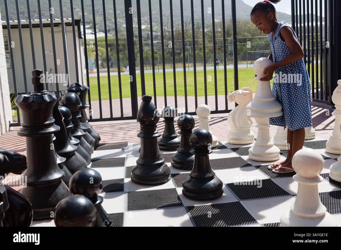 African American child placing giant white pawn on chessboard patio ...
