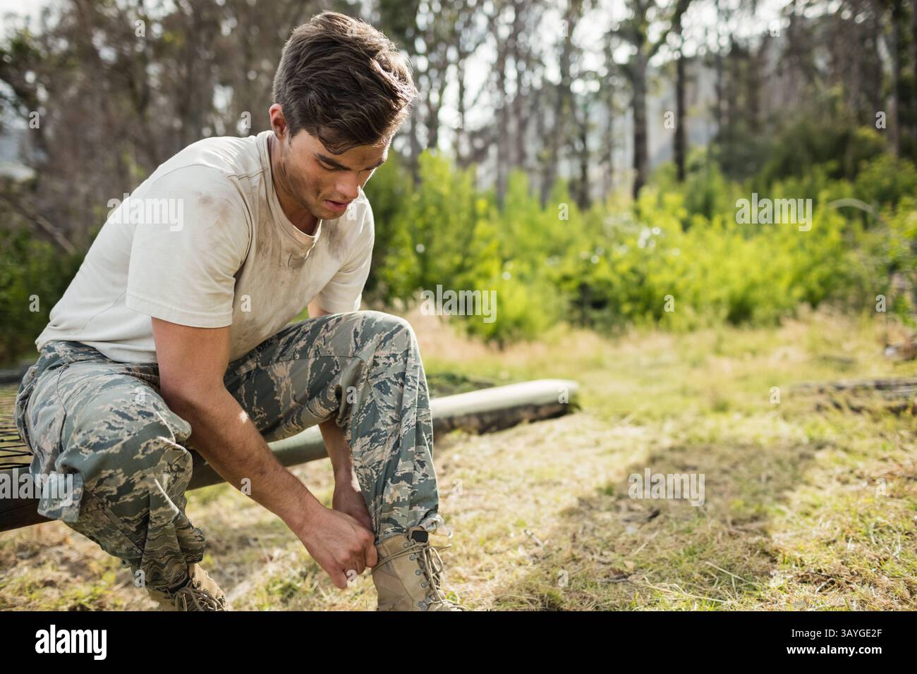 Male soldier tying tan combat boot laces on wooden beam in forest ...
