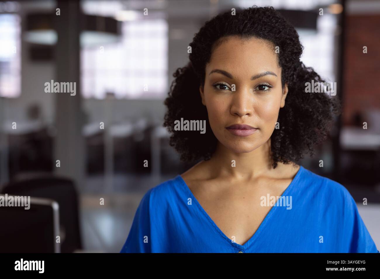 Young woman standing and looking at camera in modern office, with glass ...