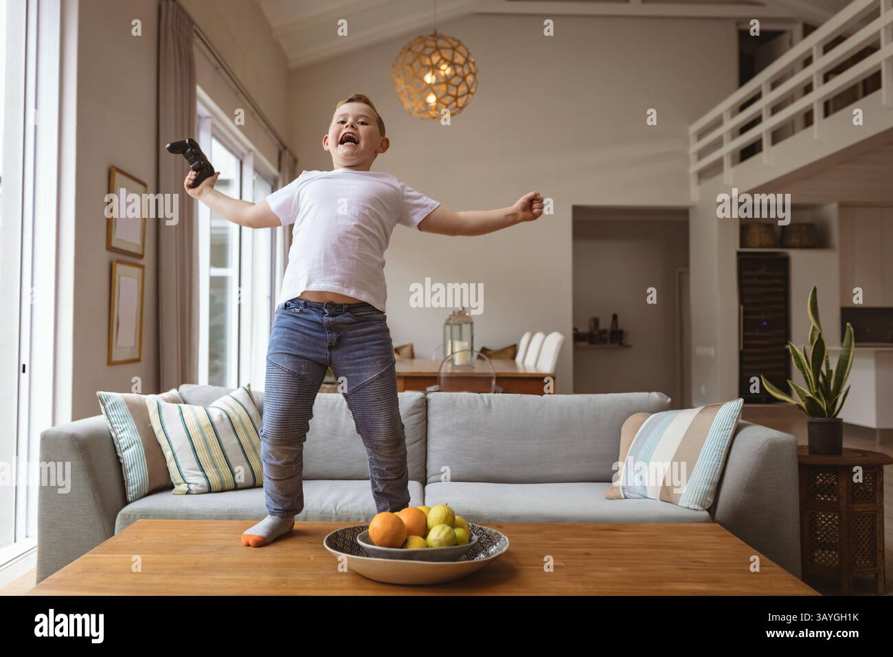 Boy jumping on sofa in open-plan living room and dining area, holding ...