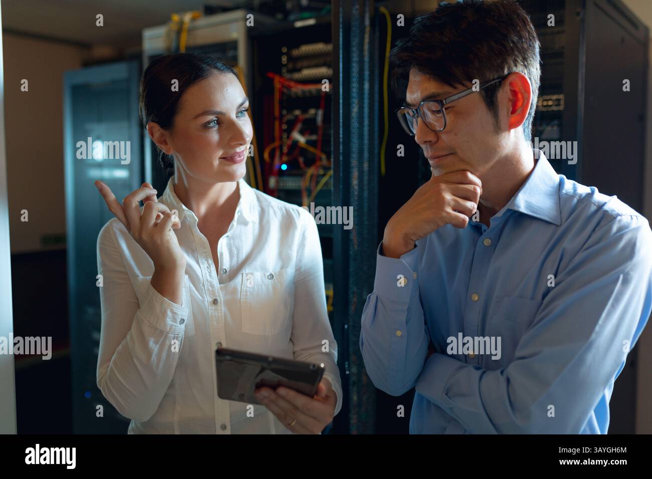 Diverse Coworkers Examining Server Racks And Cables With Blinking Leds In Server Room Using
