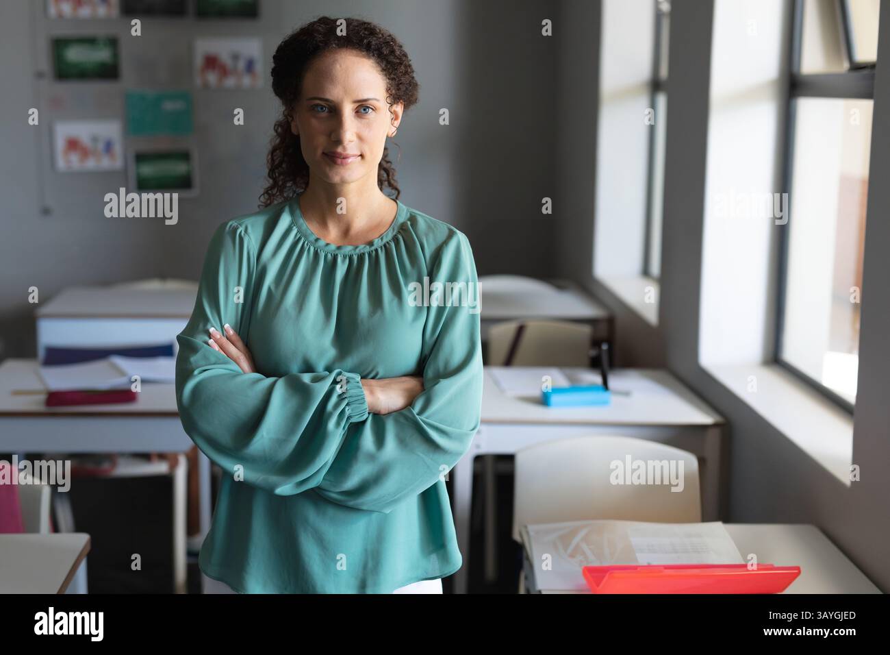 Woman standing at front of classroom, surrounded by desks notebooks and ...