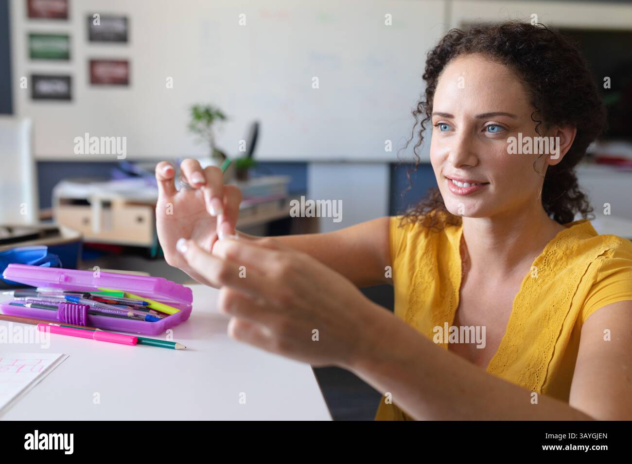 Female instructor examining small object at desk in classroom, with ...