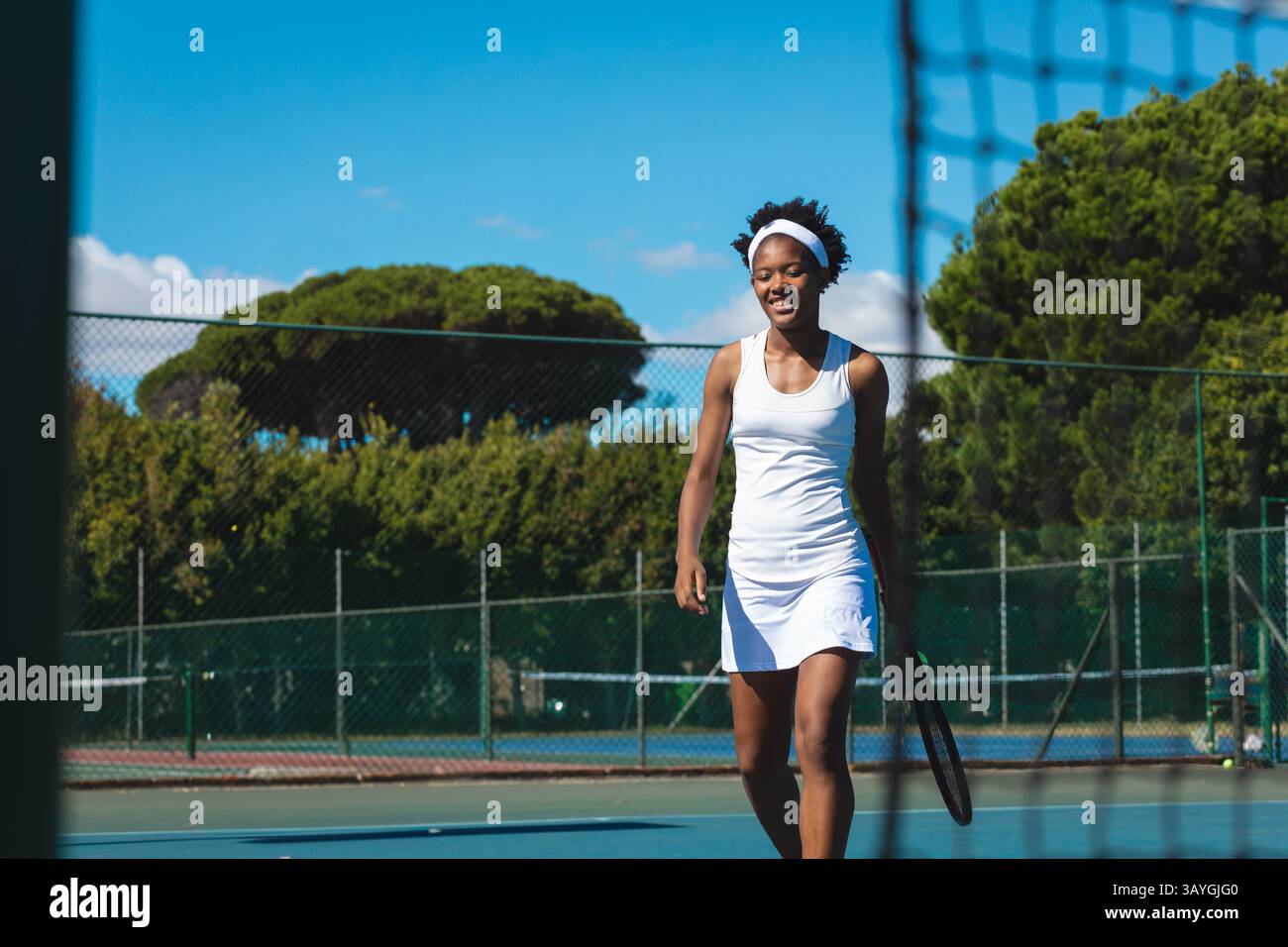 Woman tennis player walking across blue outdoor tennis court by net ...