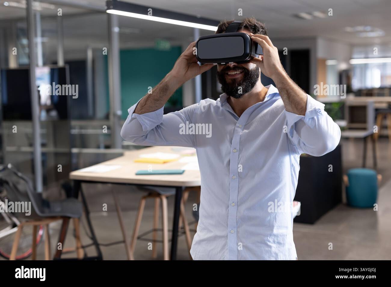 Young adult man adjusting VR headset in open?plan office, with high ...