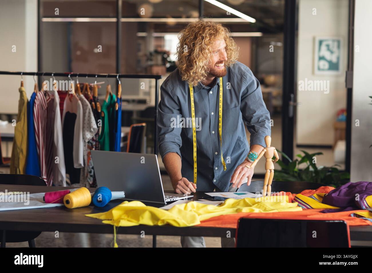 Mid-adult man designing patterns in modern fashion studio, using measuring tape and laptop Stock ...