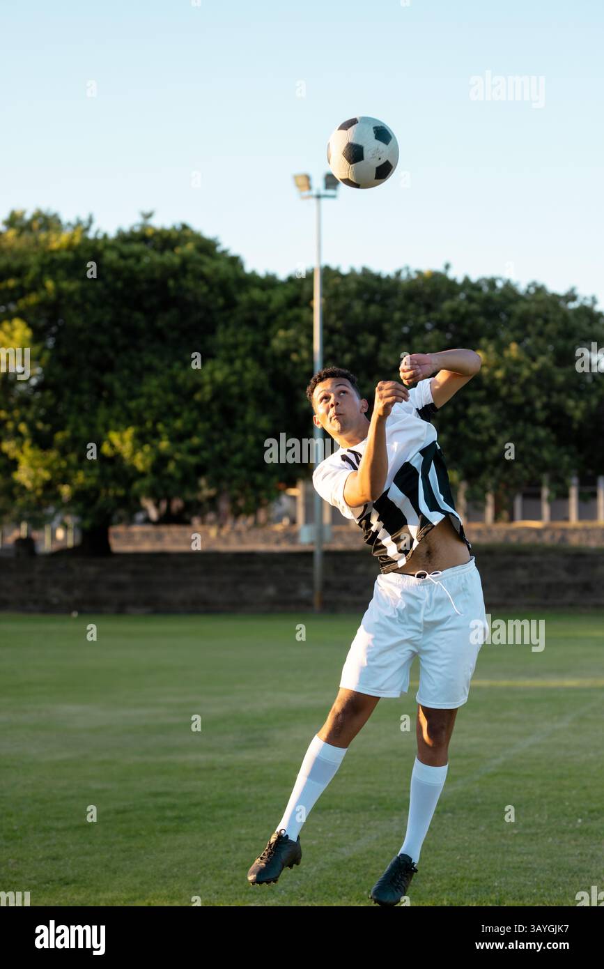 Young adult male athlete leaping in mid-air on grass soccer pitch ...