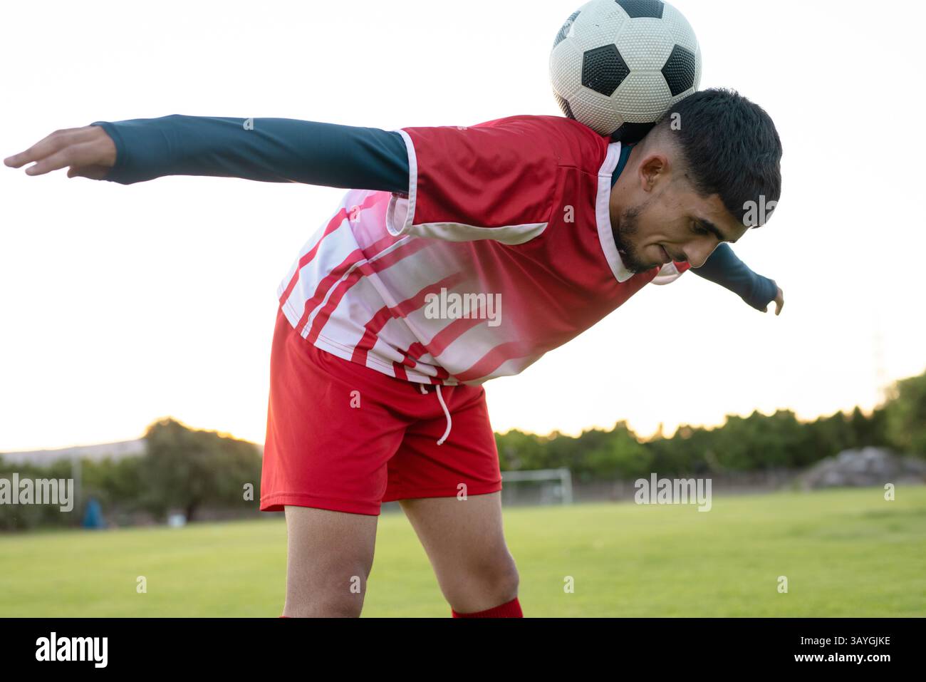 Male soccer player balancing black-and-white ball on back at grassy ...