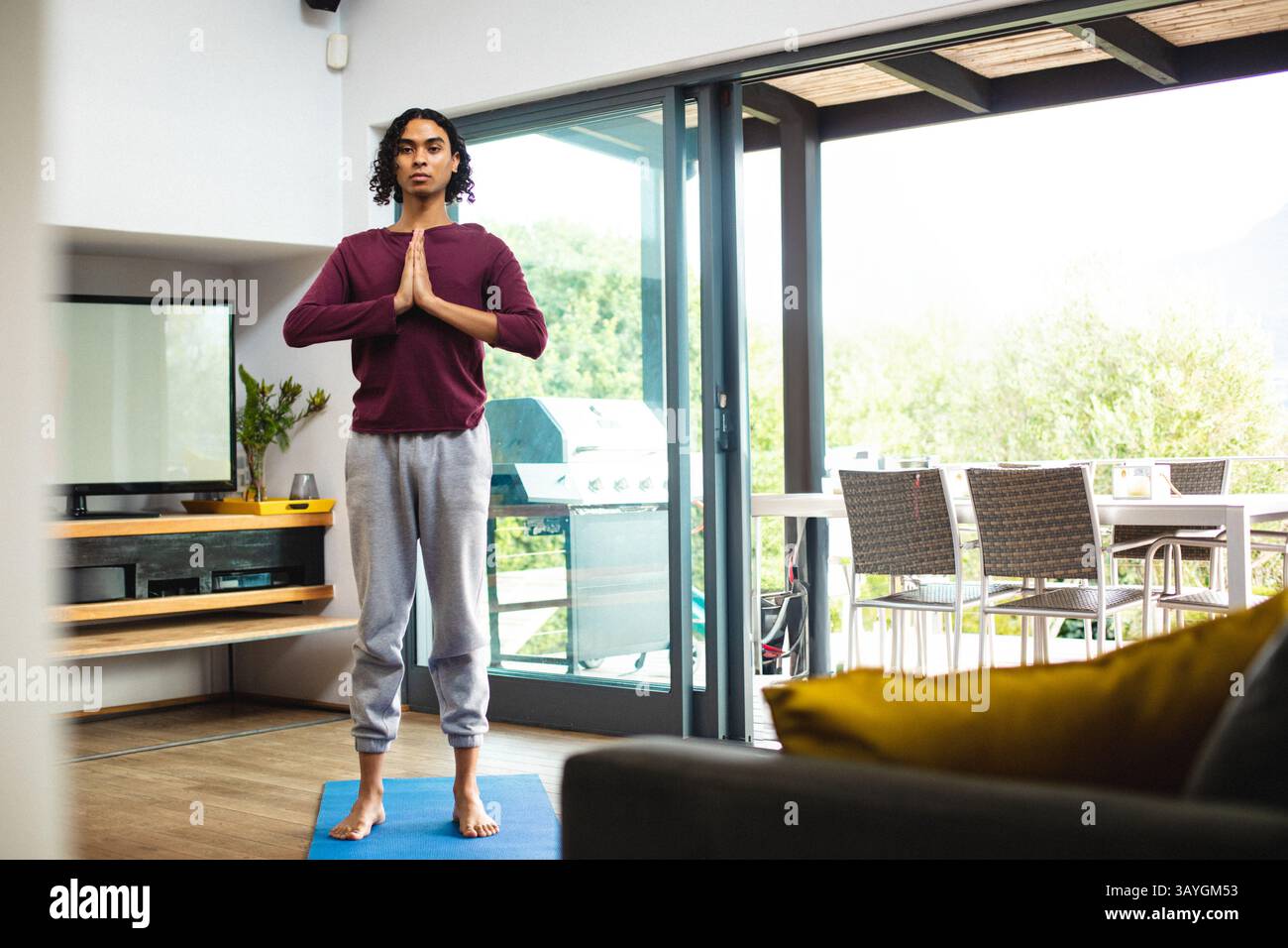 Non-binary person doing yoga prayer pose on blue mat in modern living ...