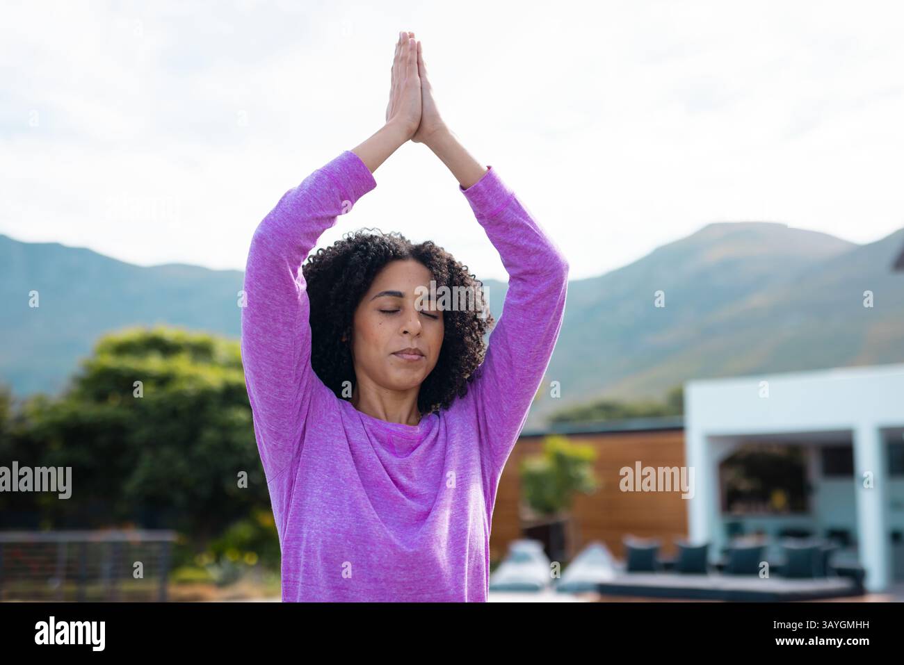 Woman doing yoga prayer pose outdoors on modern patio, with green ...