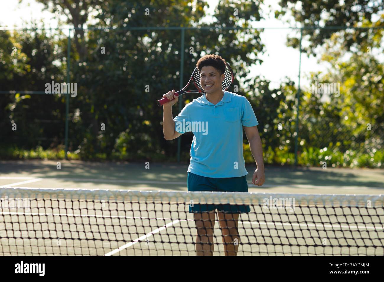 Mid-adult man standing behind tennis net on outdoor court, holding ...