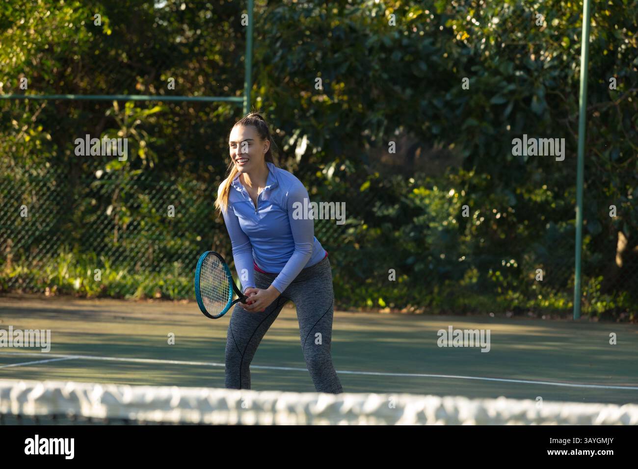 Young adult woman gripping tennis racket in ready stance on tennis ...