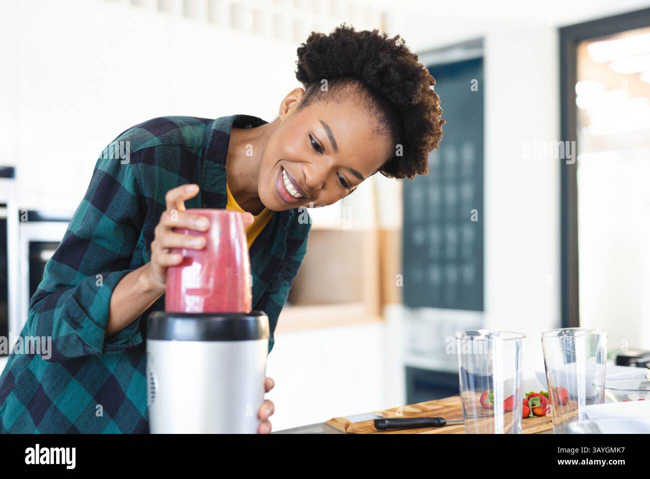 Black young adult woman placing blending cup on blender base in home ...