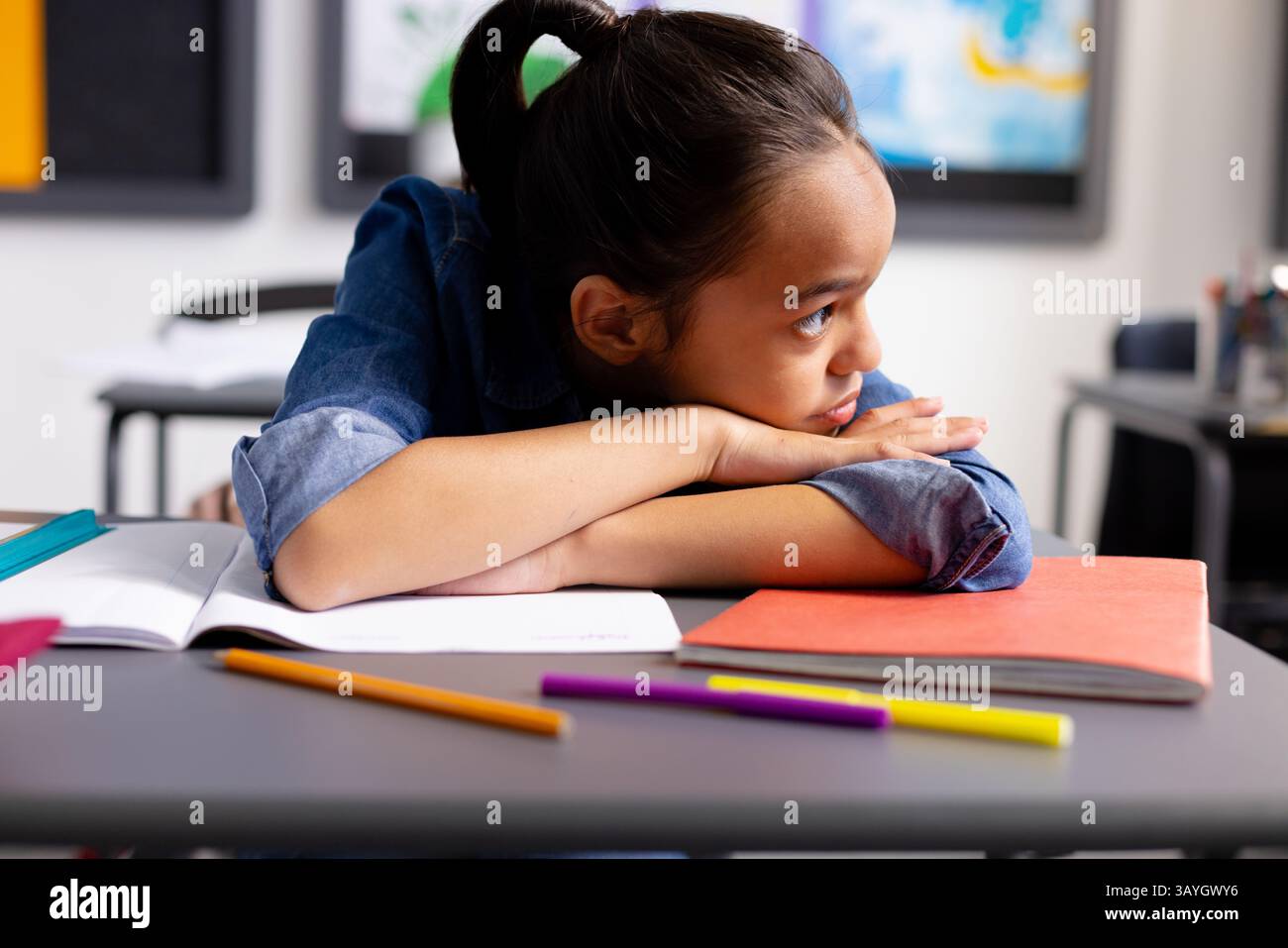 Asian child resting head on desk in classroom, gazing toward maps with ...
