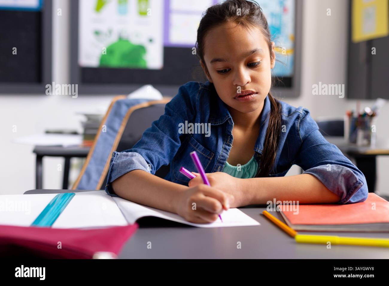 Child girl writing with purple pen in notebook at elementary classroom ...